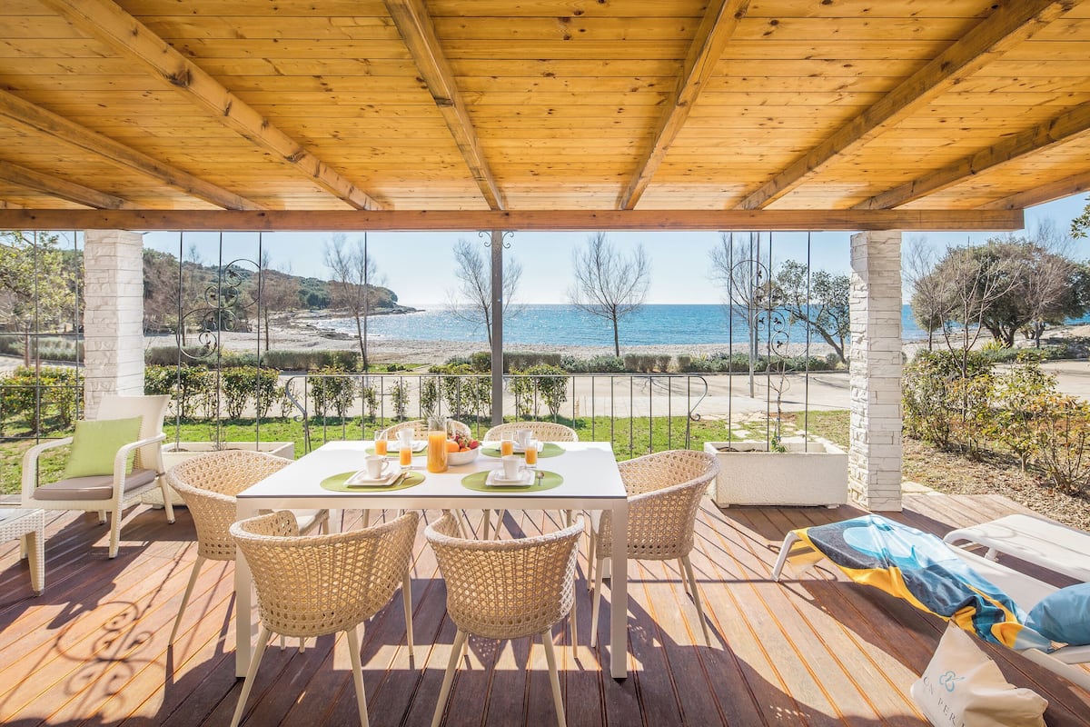 Uma área de estar coberta ao ar livre, com uma mesa posta para dois, com vista para a praia.
