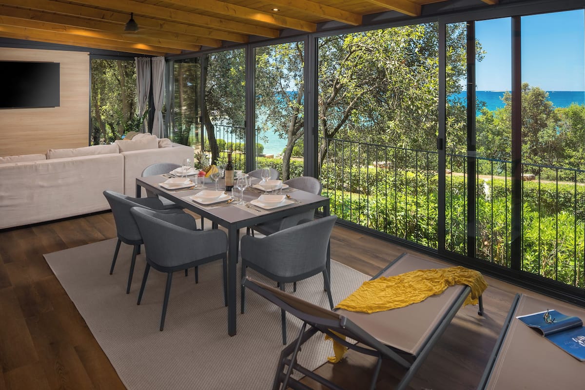 Uma zona de refeições moderna com uma mesa posta para quatro, um sofá e uma grande janela com vista para o mar.