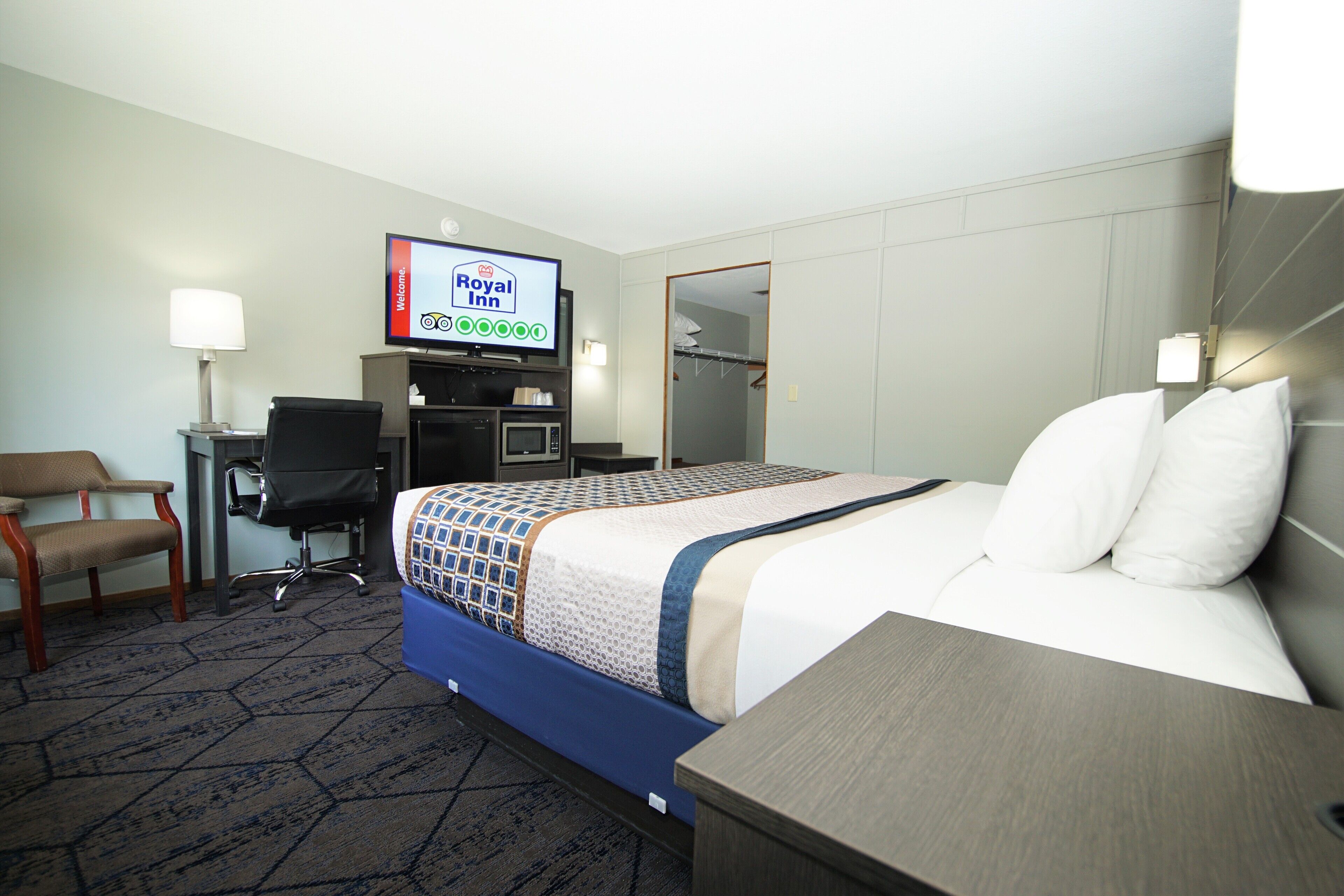 Quarto de hotel com cama, escrivaninha com computador, cadeira, televisão na parede e espelho.