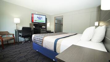 Quarto de hotel com cama, escrivaninha com computador, cadeira, televisão na parede e espelho.