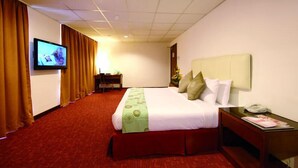 Quarto de hotel com cama, televisão na parede, escrivaninha e telefone.