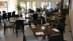 Um restaurante amplo, com várias mesas e cadeiras, janelas grandes e um design de teto moderno.
