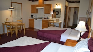 Quarto de hotel com duas camas, uma mesa, uma kitchenette e um banheiro.