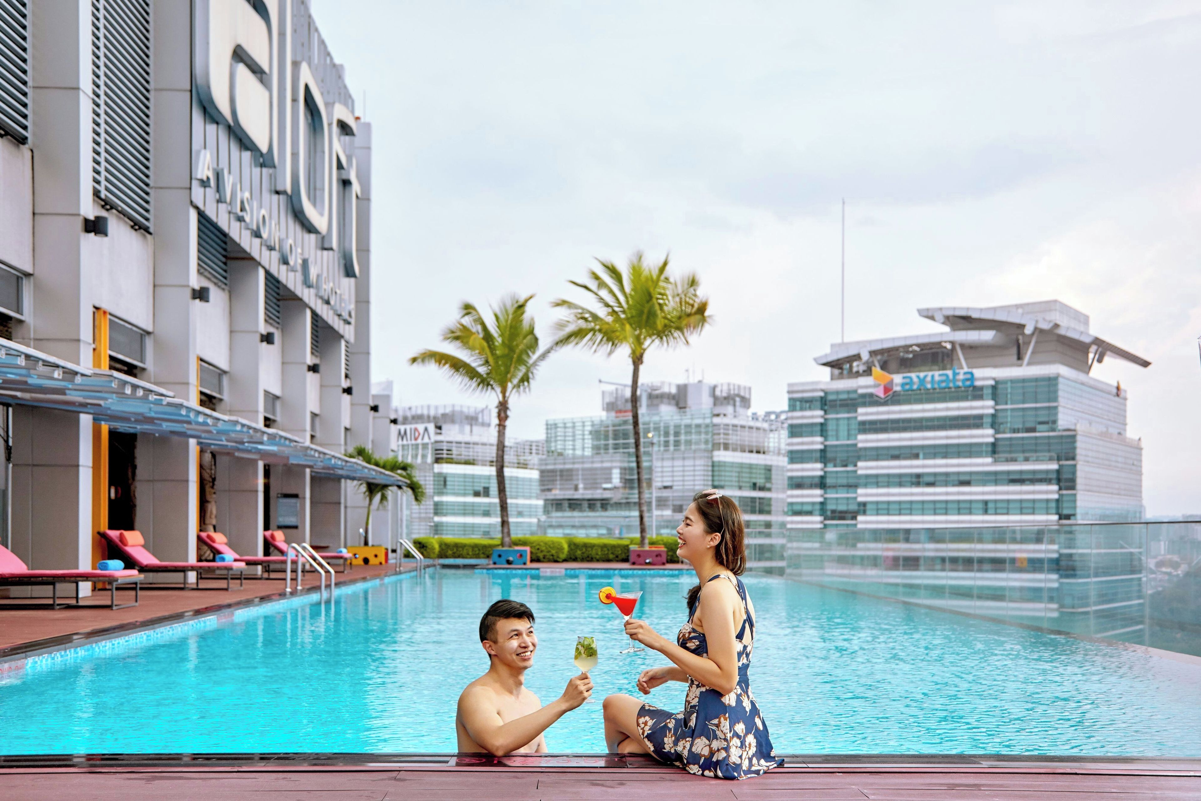 Área da piscina com espreguiçadeiras e um edifício com design moderno ao fundo.