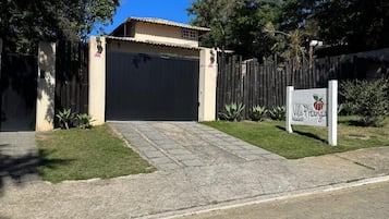 Entrada de propriedade com portão, um caminho de acesso pavimentado, uma placa e área cercada com vegetação.