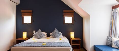 Quarto com uma cama grande, duas mesas de cabeceira com luminárias, um sofá pequeno e uma janela com vista.