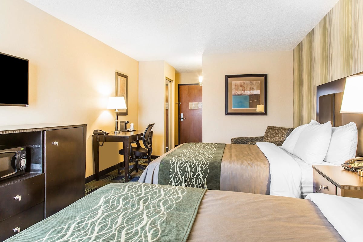 Quarto de hotel com duas camas, uma escrivaninha com luminária, micro-ondas e televisão.