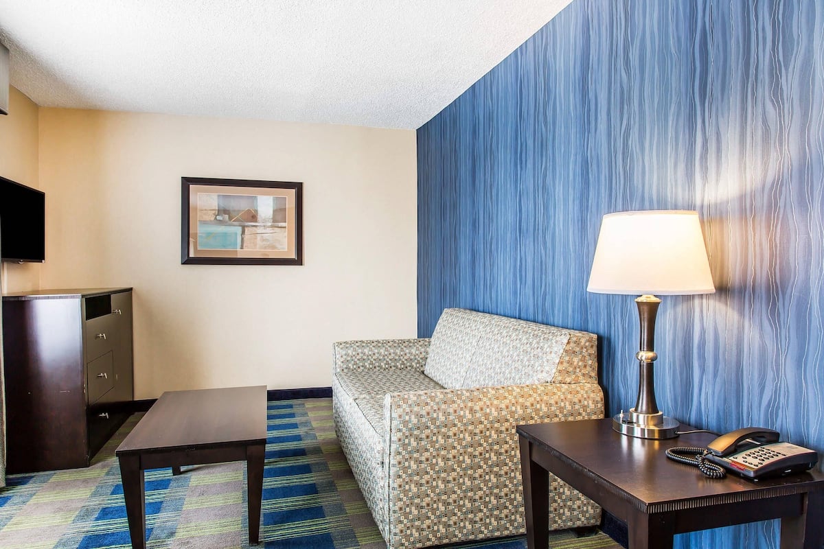 Quarto de hotel com sofá, mesa pequena, abajur, telefone e televisão sobre um móvel.