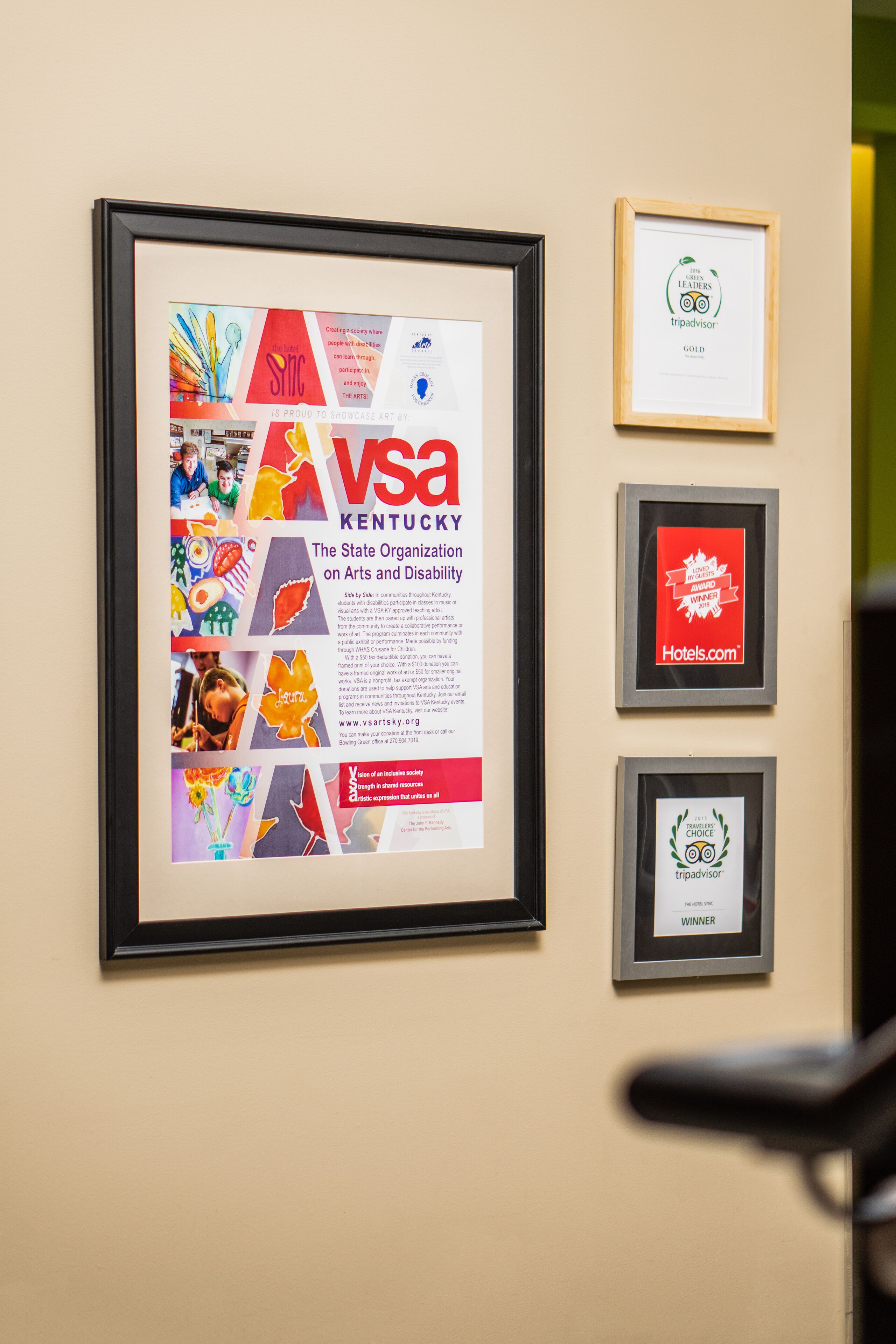 Um cartaz da VSA Kentucky emoldurado numa parede, acompanhado por dois prêmios emoldurados.