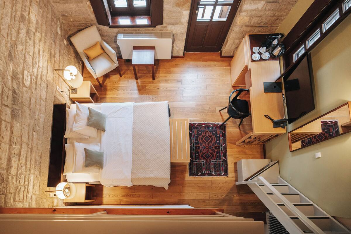 Quarto com cama, escrivaninha, cadeira, mesa pequena, abajur, televisão e escada.