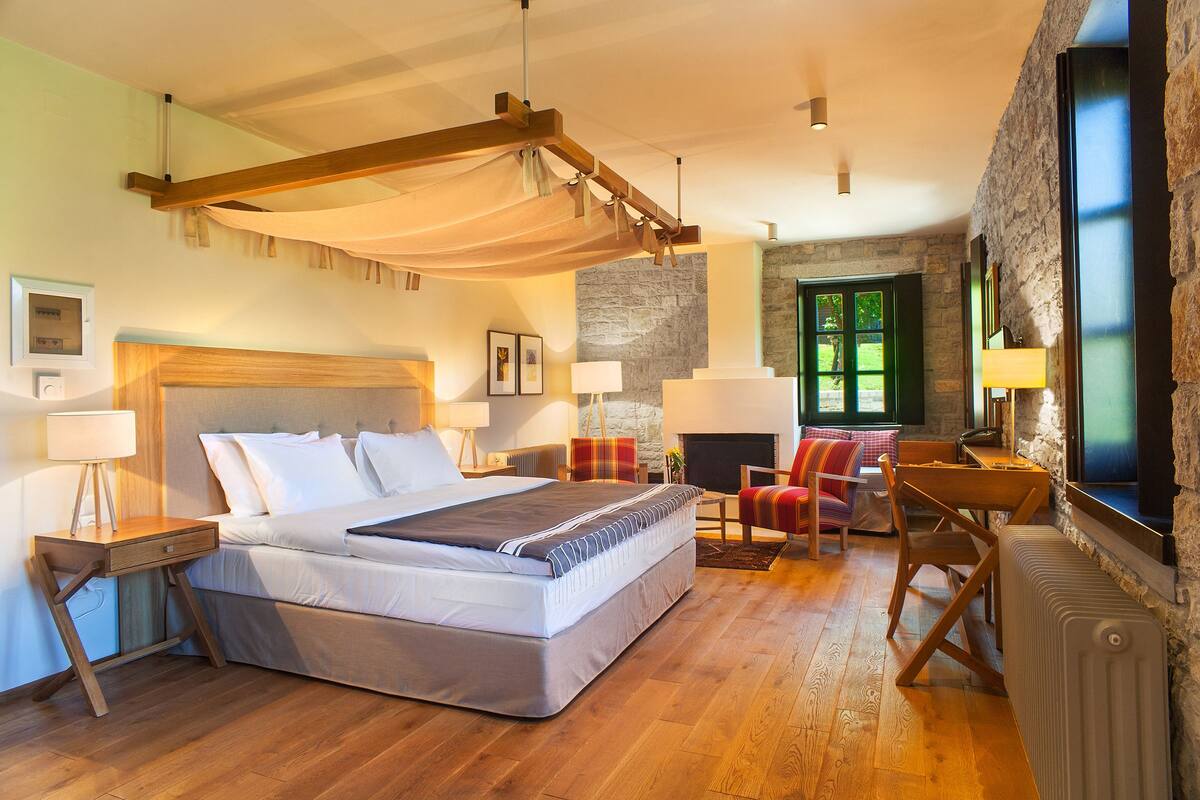 Um quarto espaçoso com uma cama grande, piso de madeira, parede de pedra e vista para o exterior.