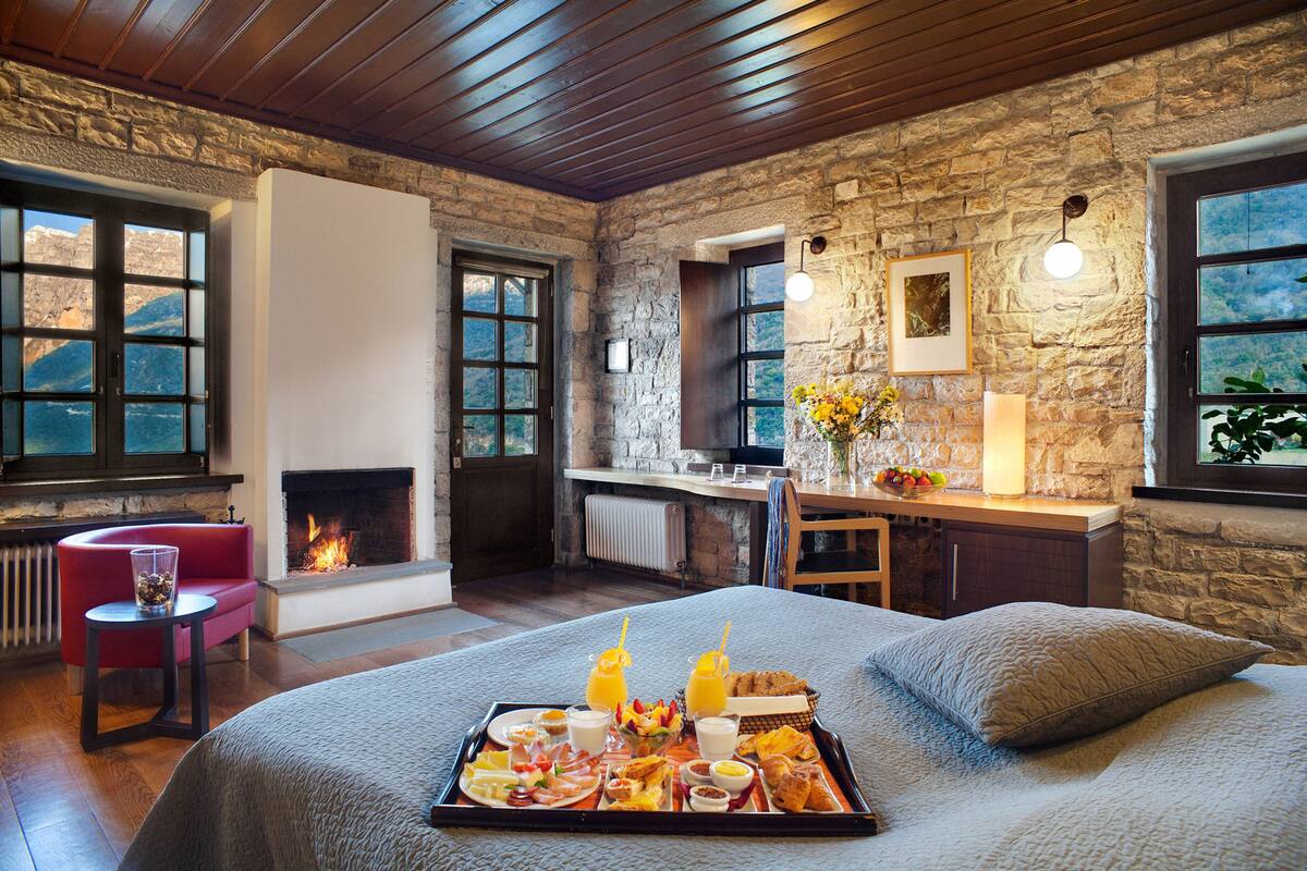 Um quarto acolhedor com lareira, paredes de pedra, cama, área de jantar e vista para o exterior.