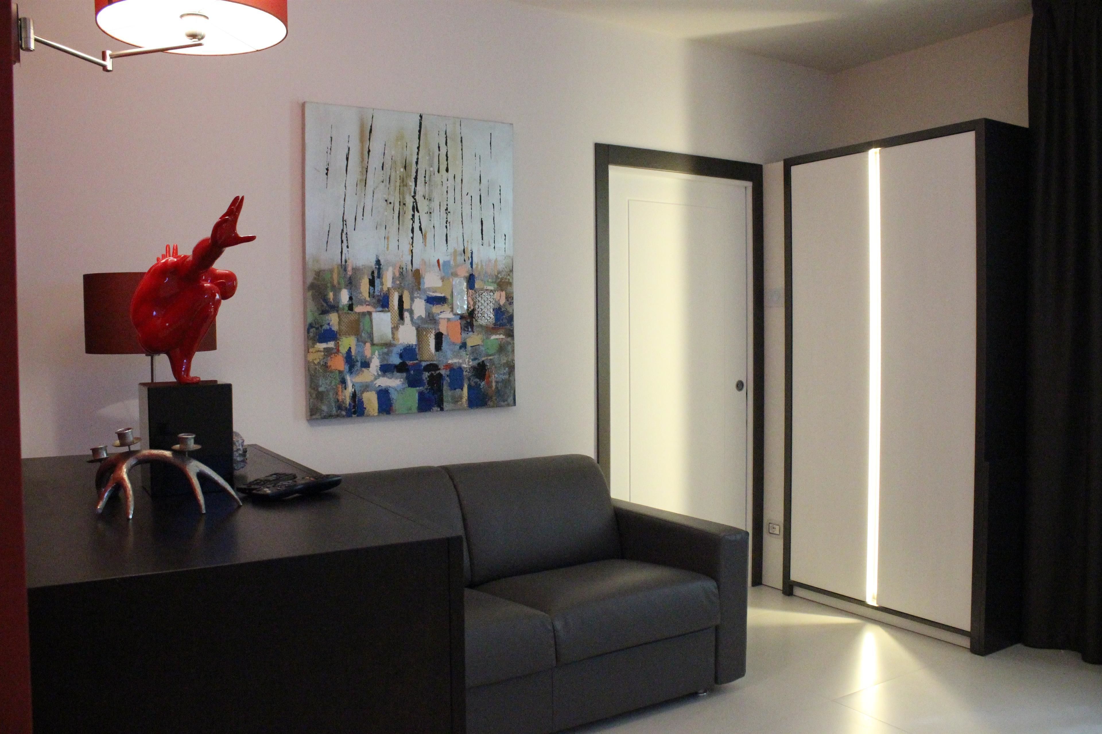 Quarto moderno com sofá cinza, uma escultura vermelha, um quadro e uma porta deslizante.
