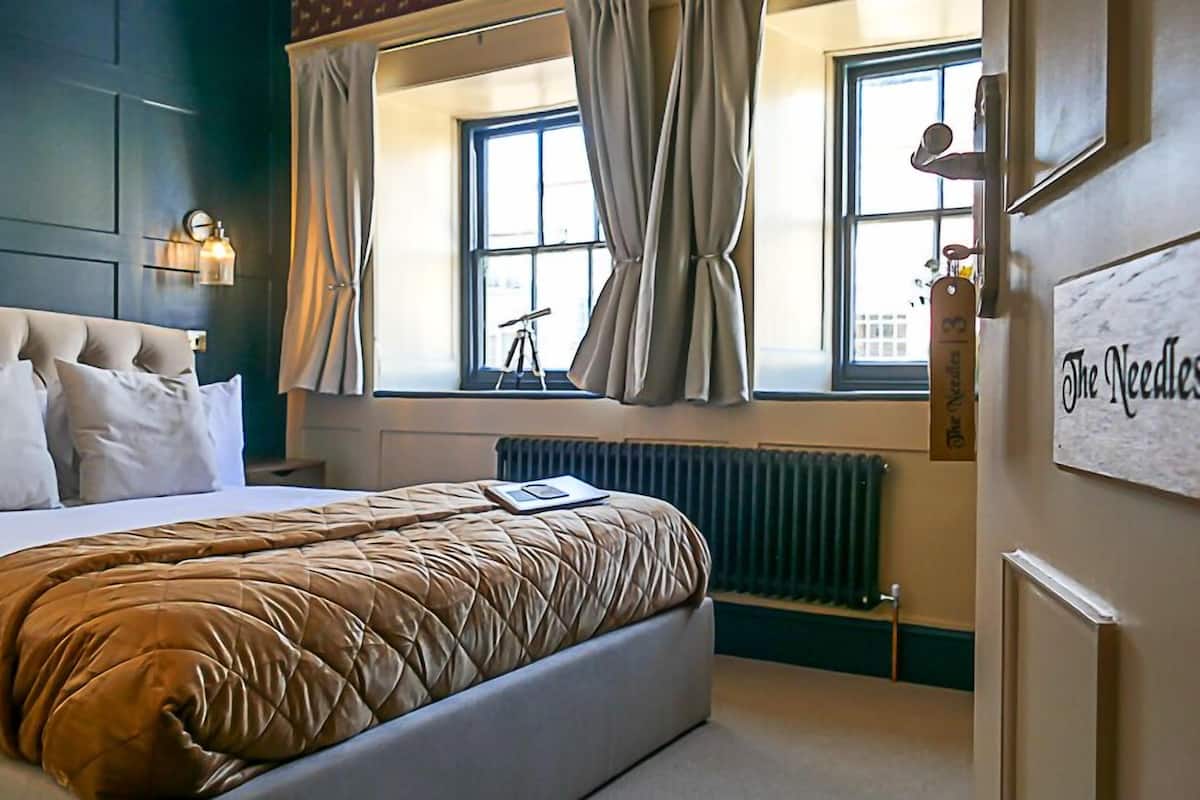 Quarto de hotel com cama grande, janela com cortinas, radiador e um aviso na parede.
