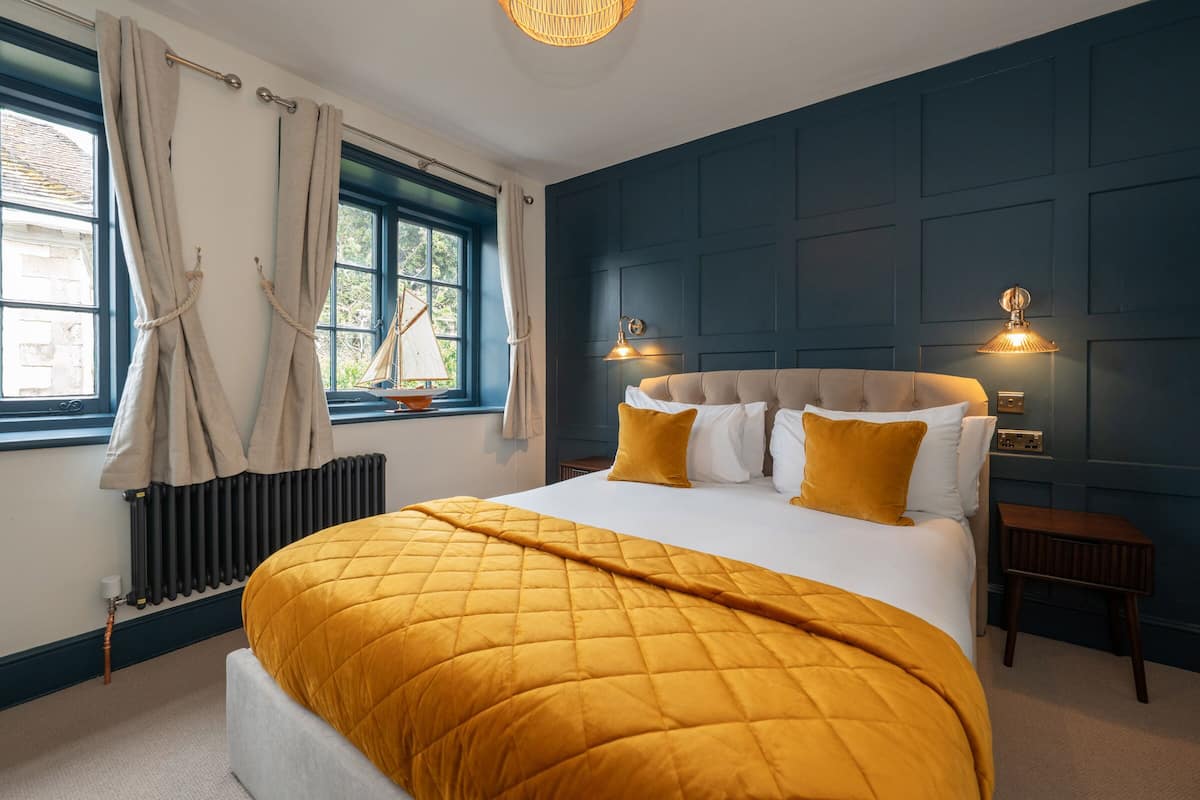 Um quarto com uma cama grande, janela com cortinas, radiador e luminárias fixadas na parede.