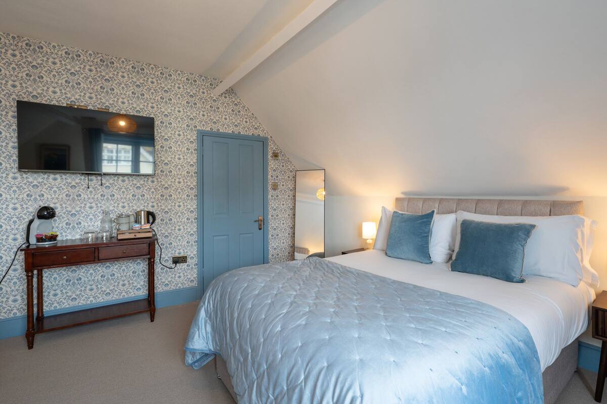 Um quarto com uma cama, uma escrivaninha, uma cadeira, um espelho e uma porta.