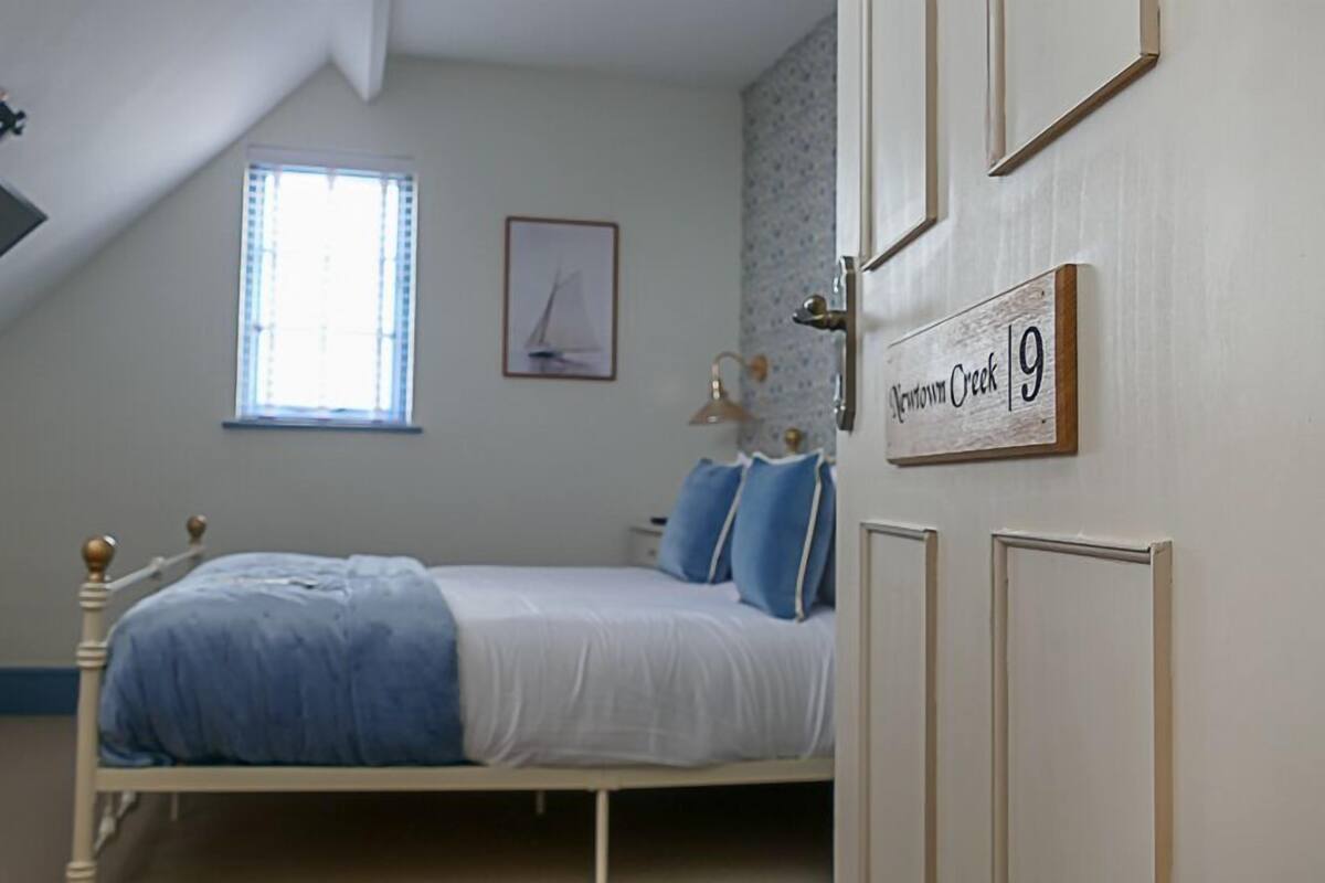 Um quarto com uma cama, uma janela, uma escrivaninha e um letreiro fixado na parede.