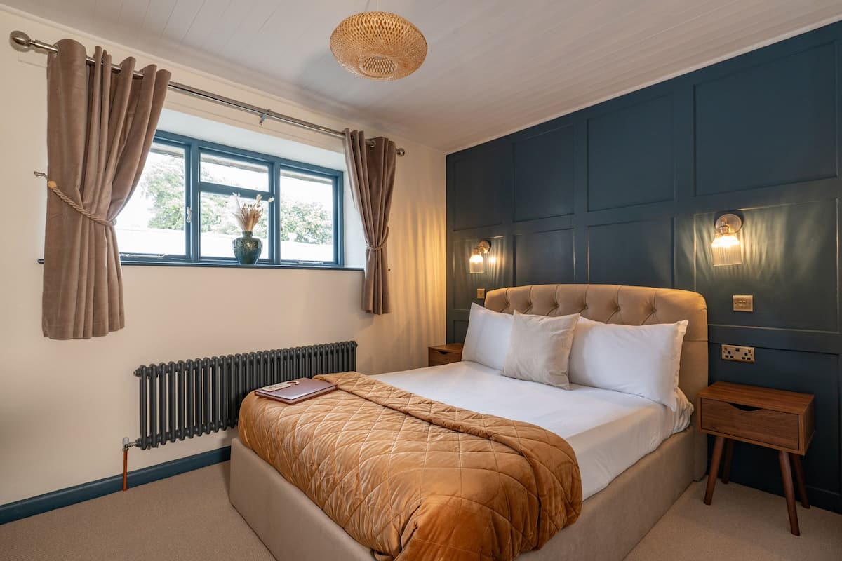 Quarto com cama grande, janela com cortinas, radiador e luzes fixadas na parede.