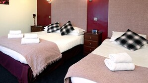Quarto de hotel com duas camas, cada uma com um edredom branco, uma manta marrom e uma almofada xadrez. Há duas mesas de cabeceira, uma com abajur e outra com relógio. As paredes são pintadas de vermelho escuro, e há um quadro pendurado na parede.