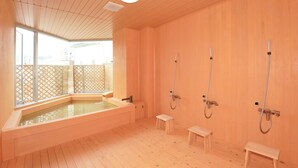 Um onsen japonês tradicional com interior em madeira, uma grande banheira de imersão e três áreas de chuveiro separadas.