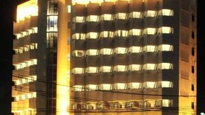 Edifício de hotel com vários andares, janelas iluminadas e uma placa grande no topo.