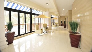 Um hall amplo com grandes janelas, assentos confortáveis e plantas em vasos.