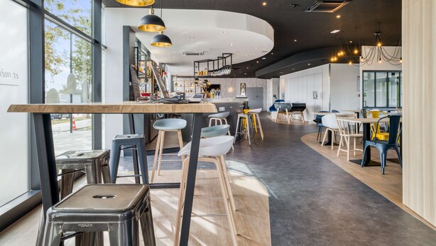Interior de restaurante moderno com tetos altos, iluminação pendente e uma mistura de banquetas de bar e mesas de jantar.