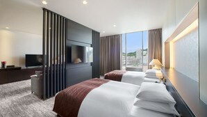 Quarto de hotel com duas camas, televisão, escrivaninha e vista da cidade.
