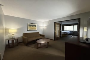 Quarto de hotel com sofá, mesinha, luminária, cama e escrivaninha.