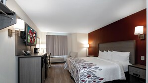 Quarto de hotel com cama, escrivaninha, televisão e luminária.