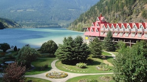 Hotel com fachada vermelha e branca, situado perto de um lago com montanhas ao fundo.