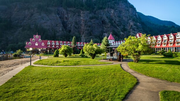 Hotel com fachada vermelha, localizado em área montanhosa com caminho claro até a entrada.