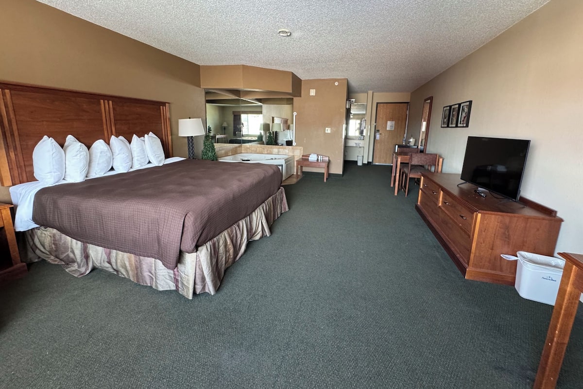 Quarto de hotel com uma cama grande, uma escrivaninha, televisão e um banheiro ao fundo.