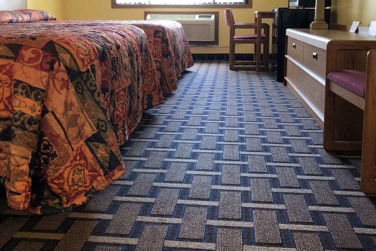 Quarto de hotel com cama, secretária, cadeira, televisão e janela.