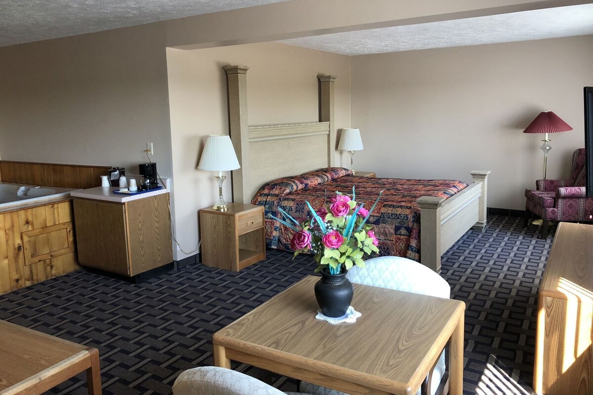 Quarto de hotel com cama, escrivaninha, cadeira, mesa pequena, vaso com flores e abajur.