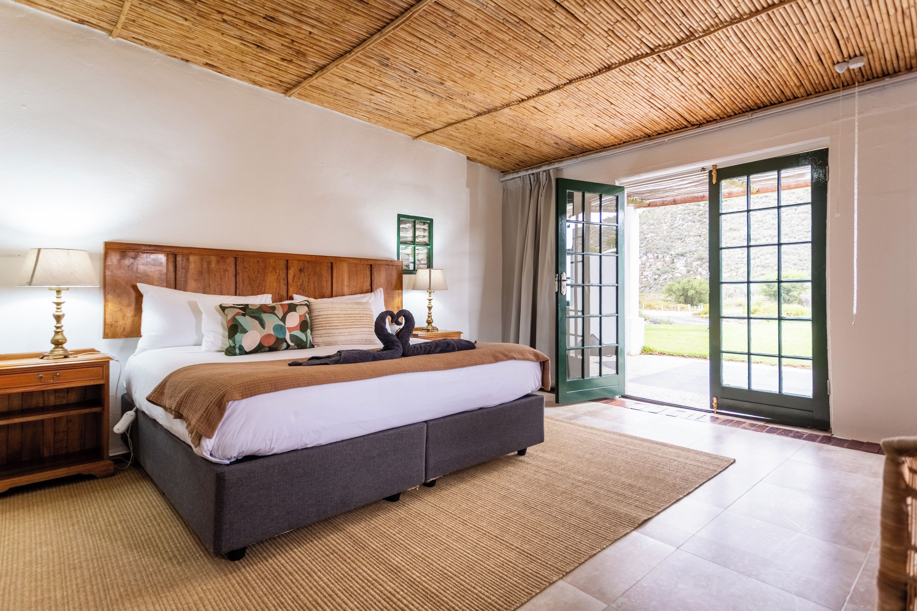 Quarto com cama grande, cabeceira de madeira, duas mesas de cabeceira com luminárias, janela com cortinas e vista para o exterior.