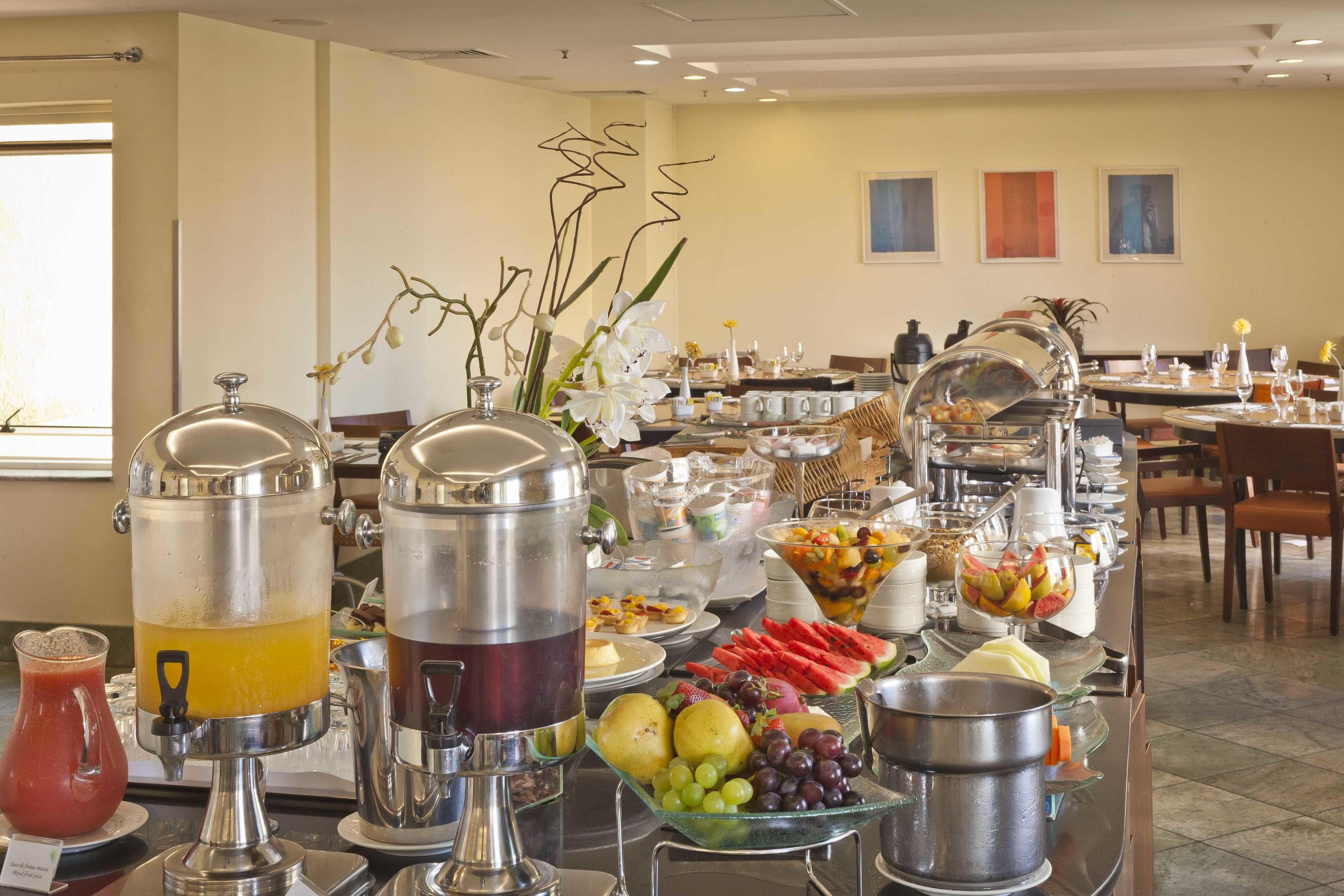 Buffet com diversos alimentos e bebidas, incluindo frutas, legumes e bebidas quentes.