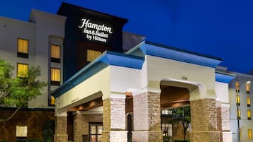 Um hotel com uma fachada de pedra e uma placa que diz 'Hampton Inn & Suites by Hilton'.