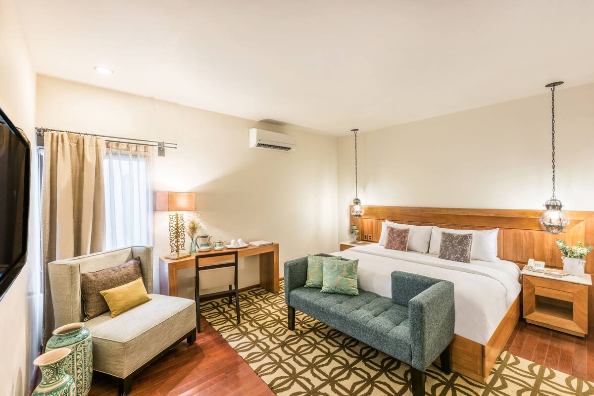Quarto de hotel com cama, sofá, escrivaninha e televisão.