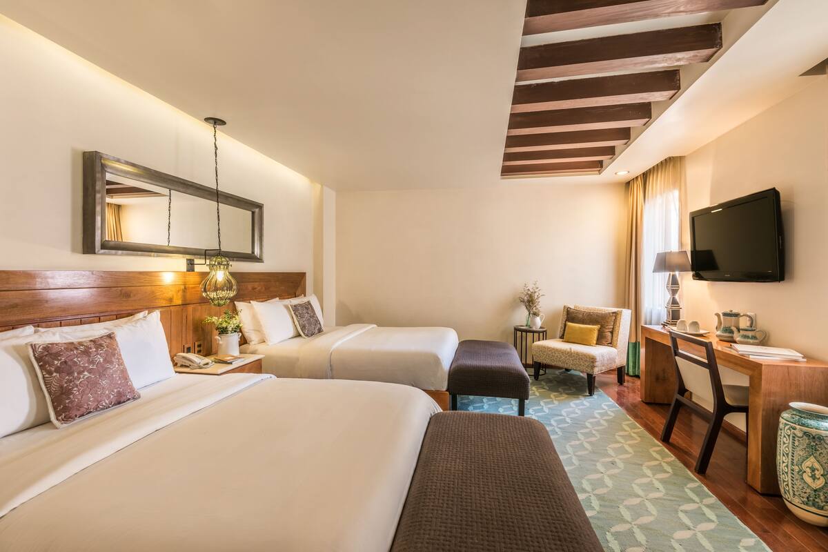 Quarto de hotel com duas camas, uma escrivaninha, televisão e um pequeno espaço de estar.