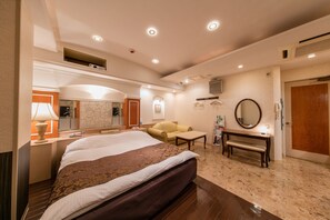 Quarto de hotel com uma cama grande, um sofá, uma mesinha, um espelho e uma porta.