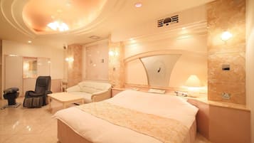 Um quarto espaçoso com uma cama grande, duas poltronas, uma escrivaninha e uma toucador com espelho.