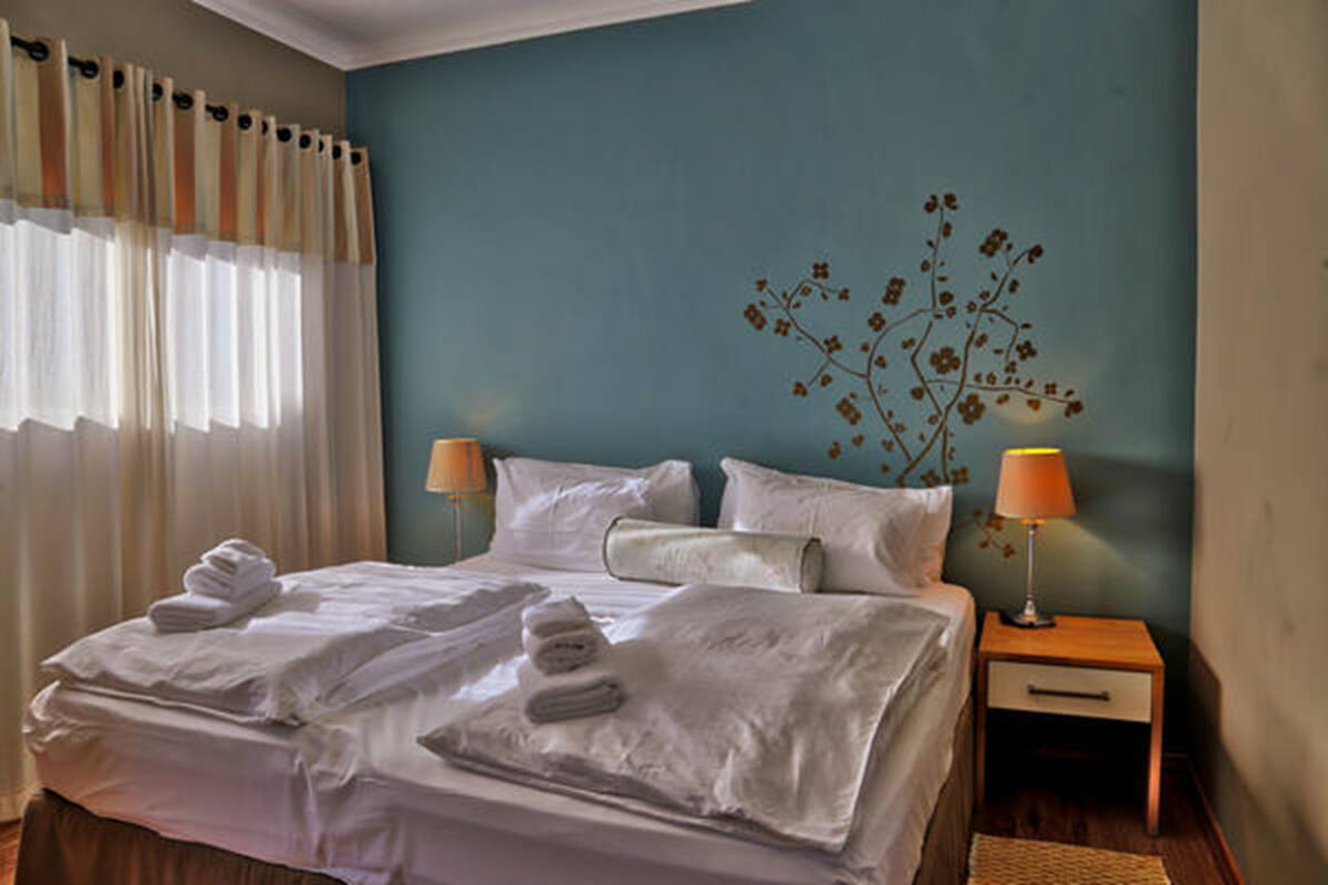 Uma cama bem arrumada com toalhas, um criado-mudo com uma luminária e uma parede com um desenho floral.