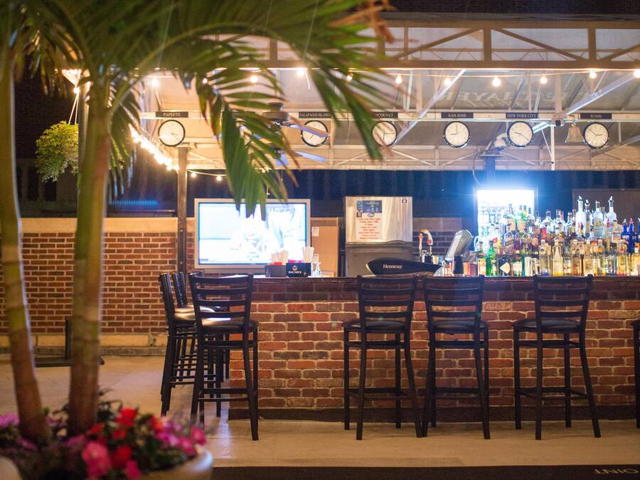 Uma área de bar com parede de tijolos, cadeiras de madeira, balcão e uma tela de televisão.