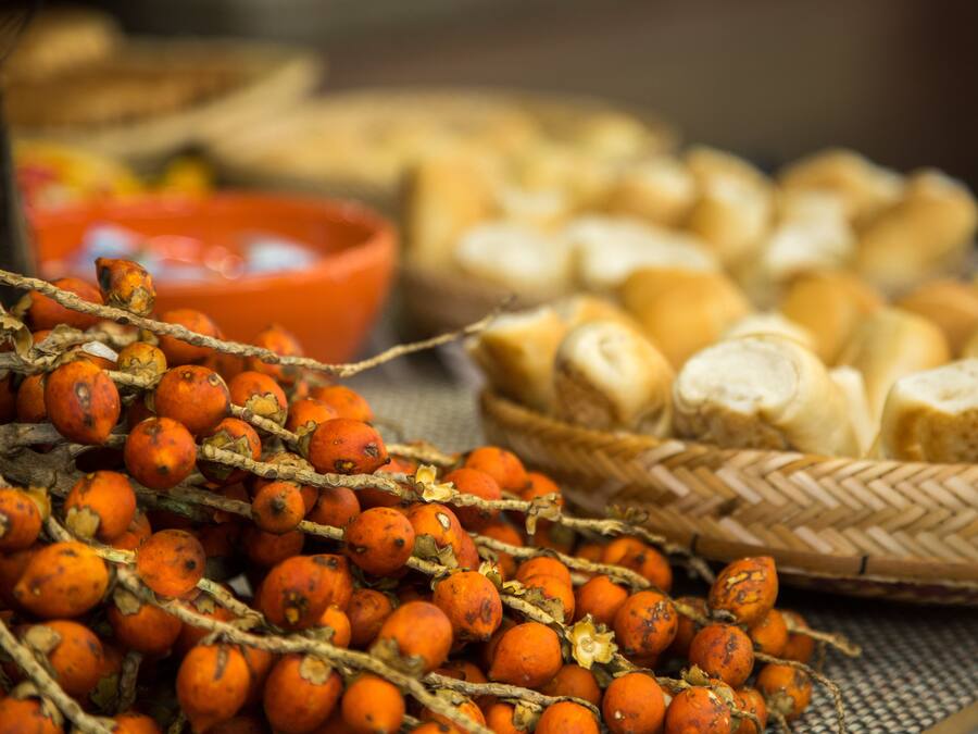 Uma mesa com cestos de frutas redondas e laranjas e uma travessa de pão.