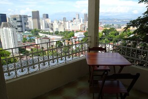 Varanda com vista para a cidade, com uma mesa e cadeiras de madeira.