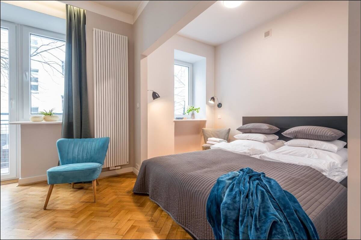 Um quarto moderno com uma cama grande, uma cadeira azul, uma janela com cortinas e um radiador.