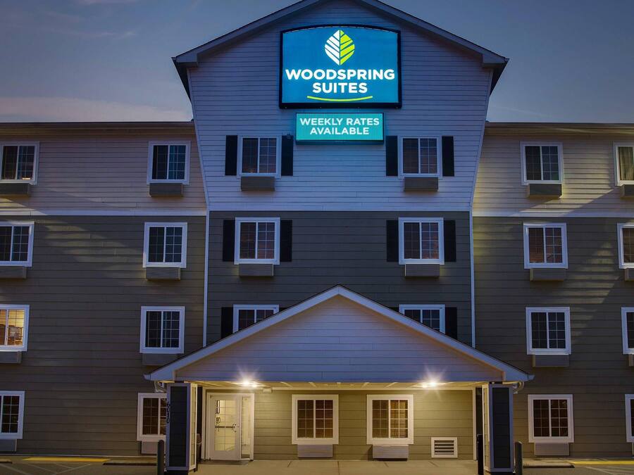 Um hotel com vários andares, com uma placa indicando 'Woodspring Suites' e 'Taxas Semanais Disponíveis'.