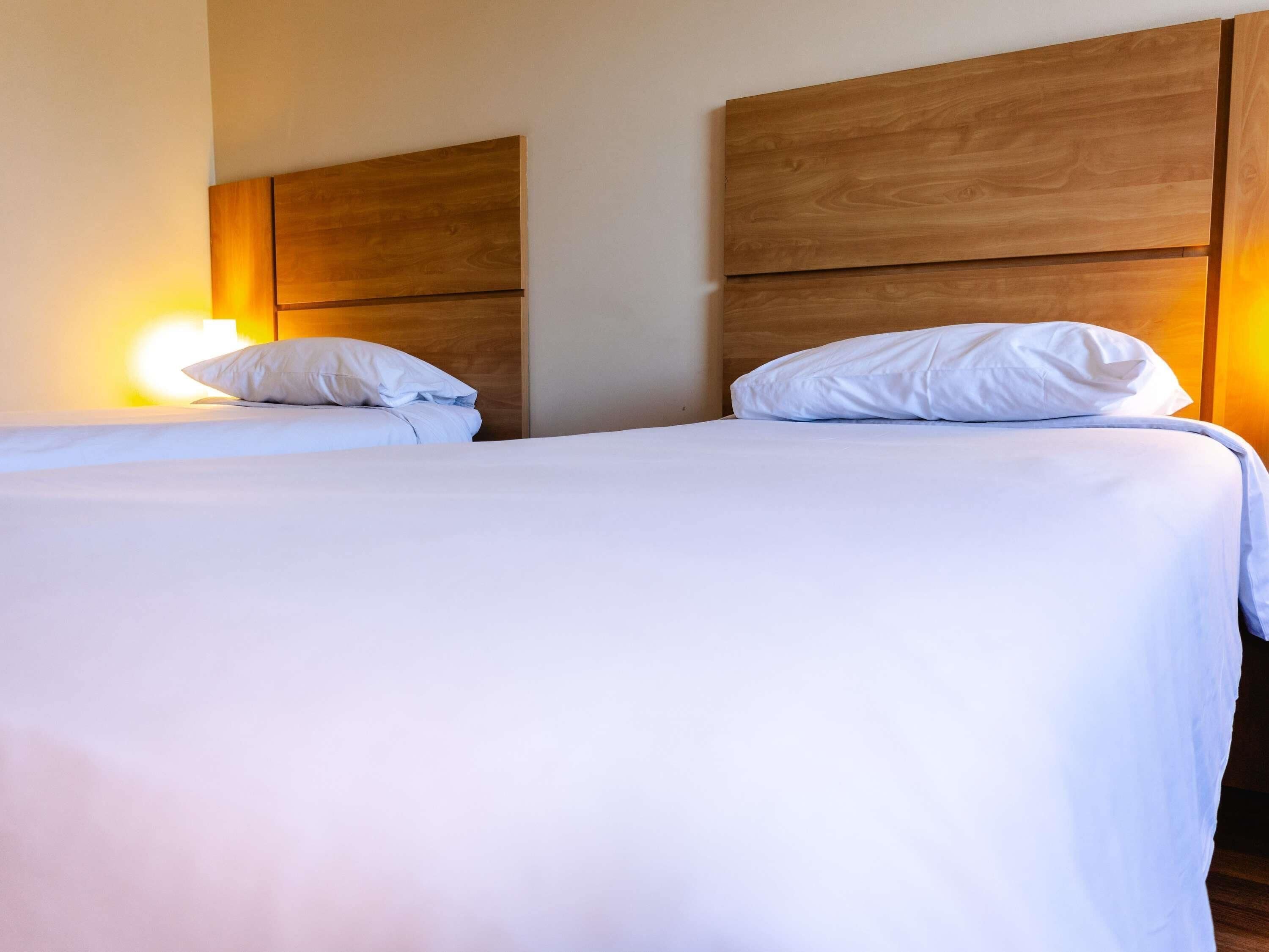 Duas camas com cabeceiras de madeira e roupa de cama branca num quarto de hotel.