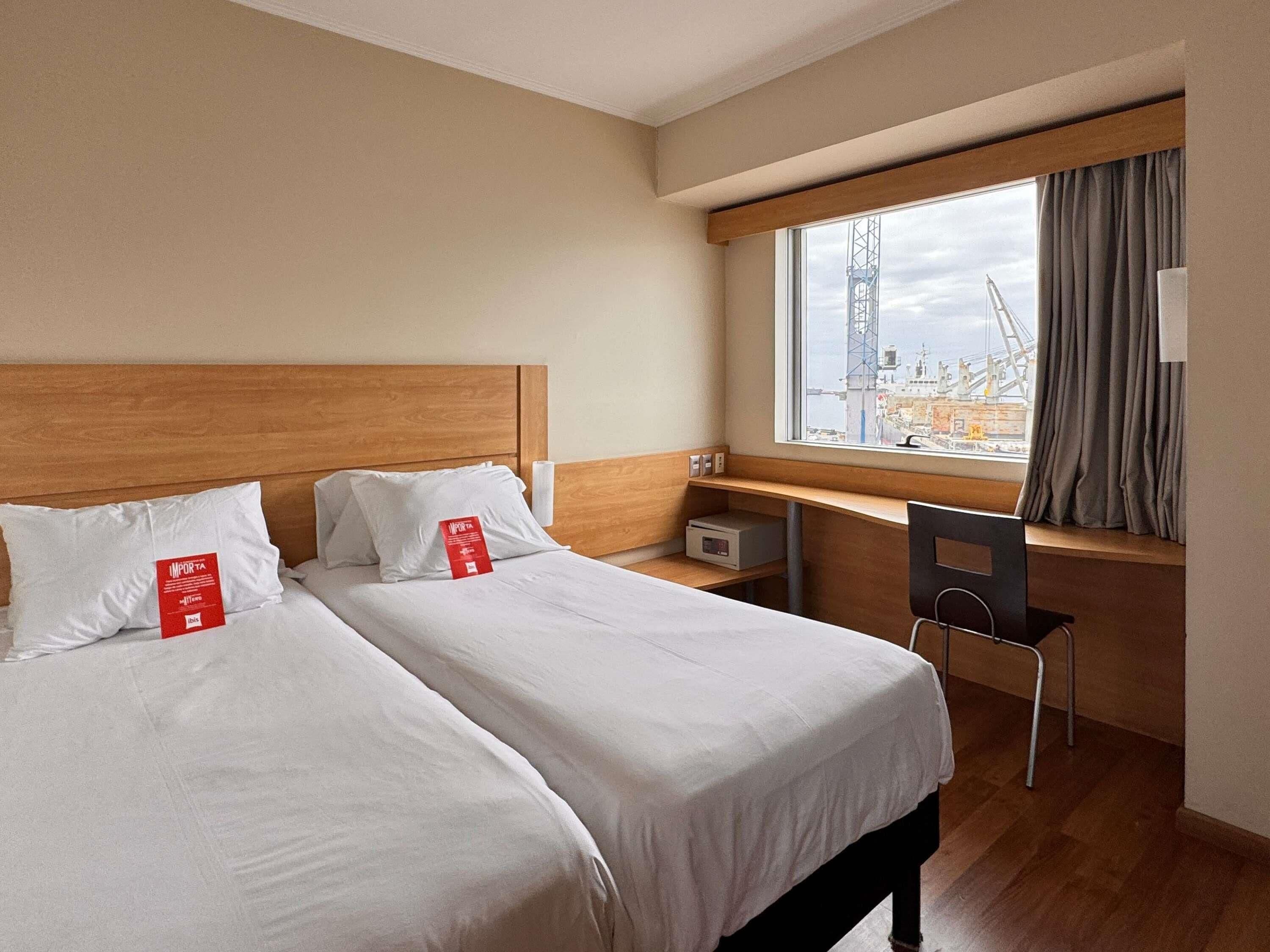 Quarto de hotel com duas camas, uma mesa e uma cadeira.